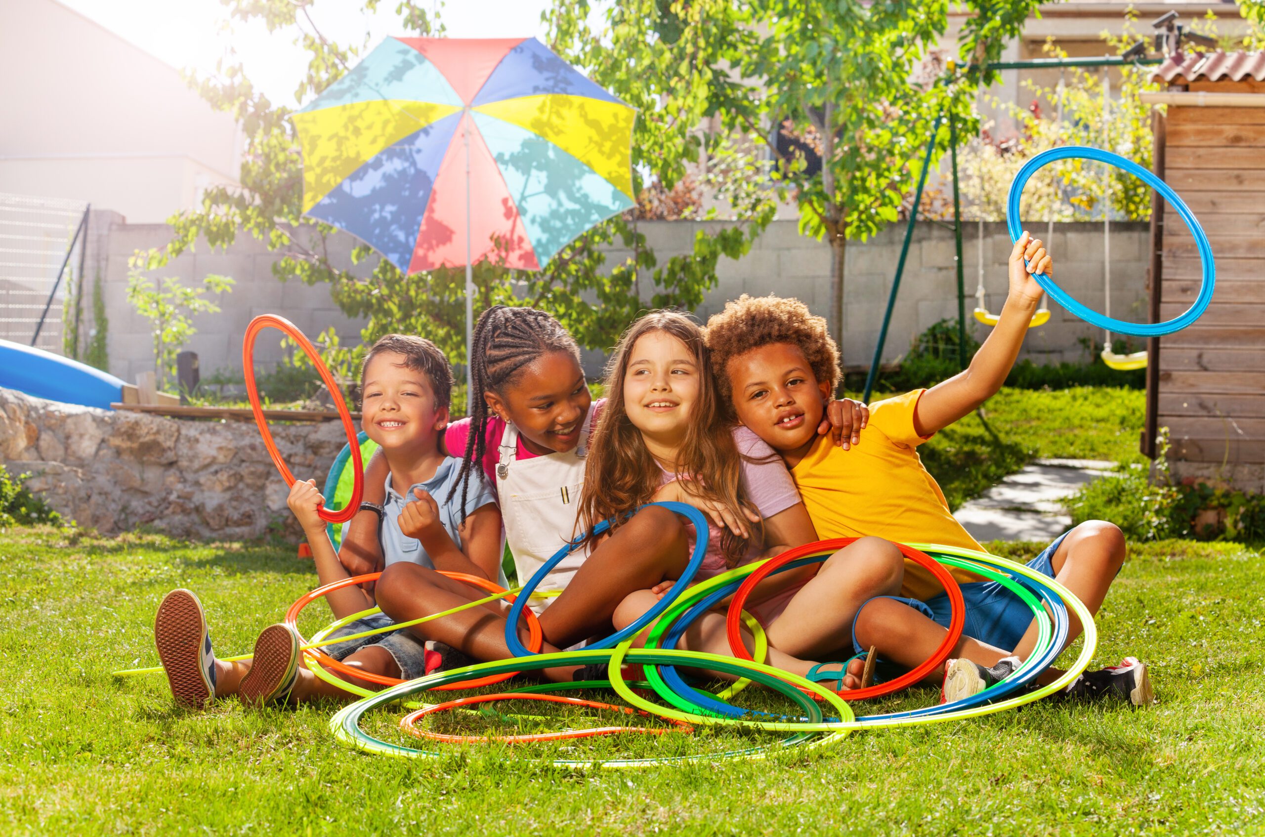 Four kids in a group sit with hula hoops on lawn - Endeavor Schools